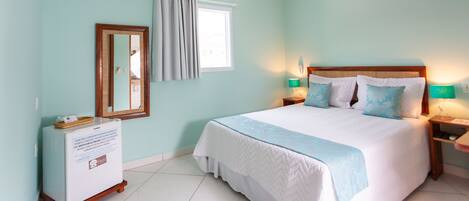 Quarto com cama, mesas de cabeceira, espelho, ventilador de teto e geladeira.