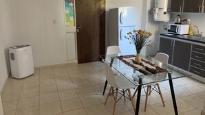 Uma cozinha moderna com geladeira, micro-ondas e dispensador de água. Há uma mesa de jantar com cadeiras e um vaso de flores.