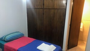 Quarto com duas camas, um guarda-roupa de madeira e um banheiro visível através de uma porta aberta.