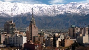 Paisagem urbana com montanhas nevadas ao fundo e vários arranha-céus em primeiro plano.