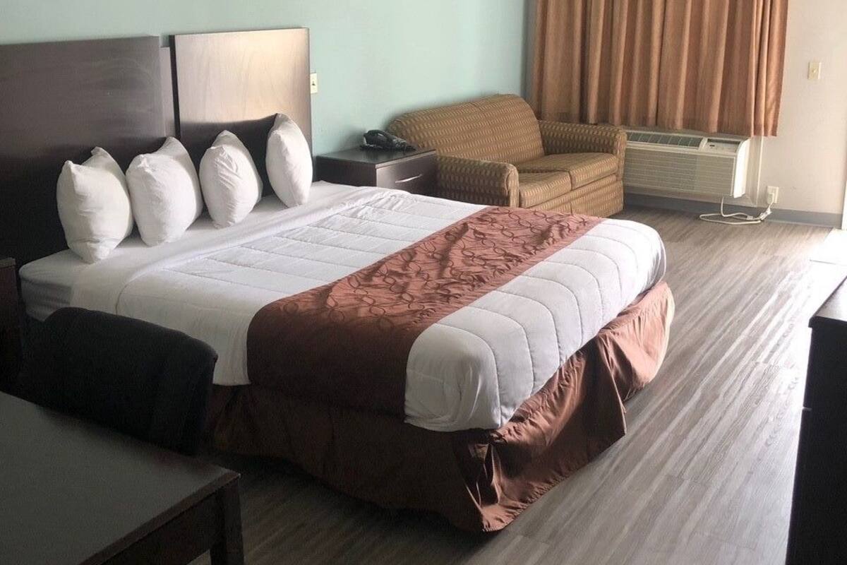 Quarto de hotel com uma cama grande, escrivaninha, cadeira e janela com cortinas.
