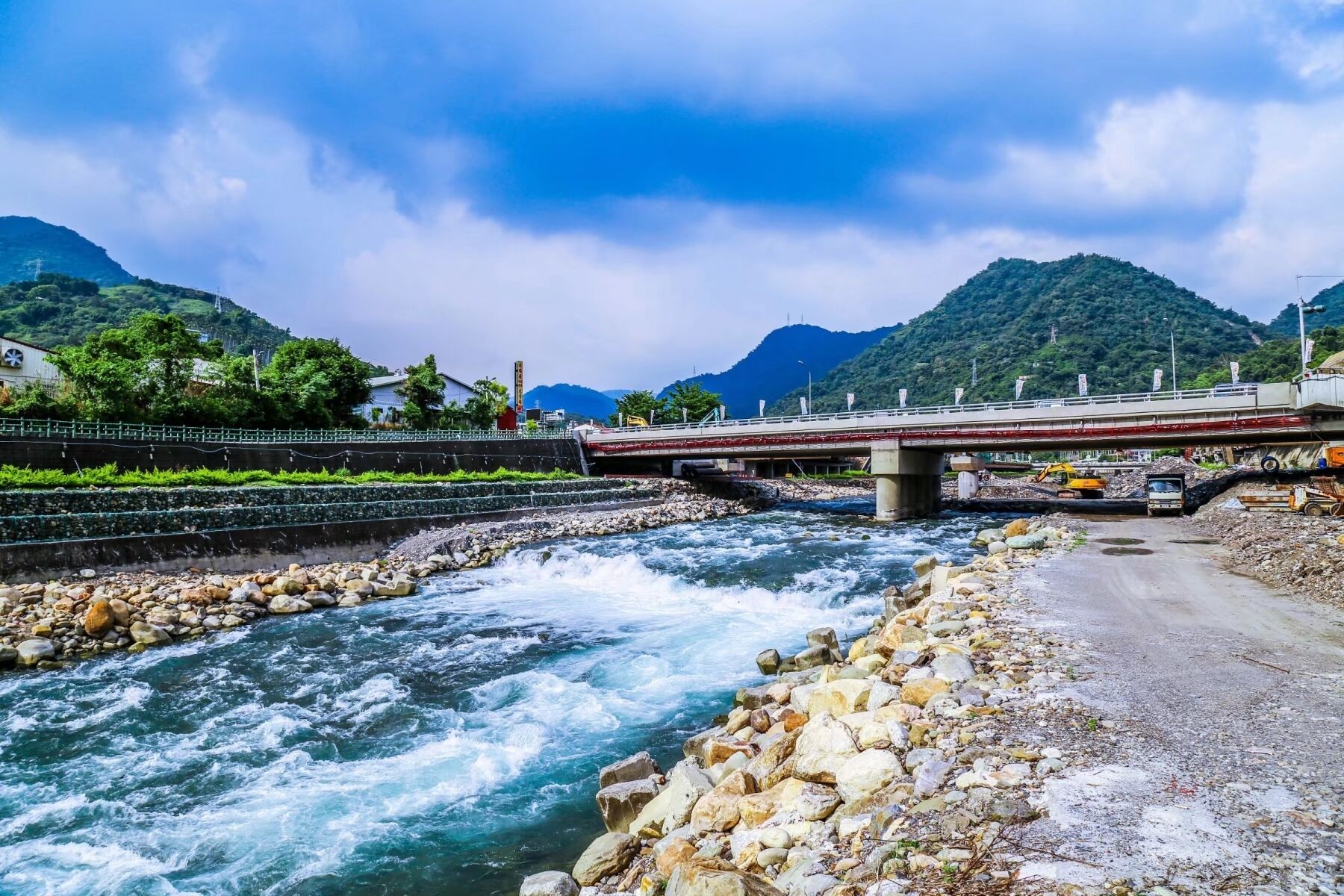 Um rio com uma ponte, margem rochosa e montanhas ao fundo.
