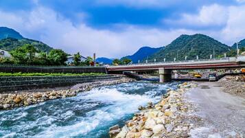 Um rio com uma ponte, margem rochosa e montanhas ao fundo.