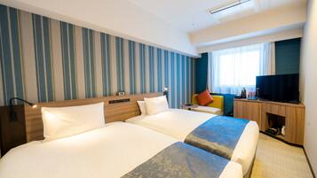 Quarto de hotel com duas camas, uma escrivaninha, televisão e janela com cortinas.