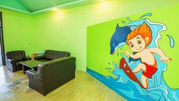 Quarto com parede verde, sofá, mesa de centro e um mural de uma criança surfando com um golfinho.