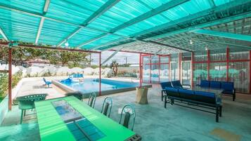 Uma área externa coberta com piscina, assentos e uma mesa.