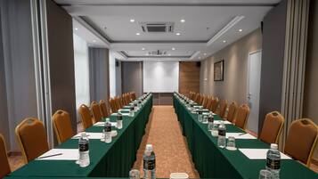 Uma sala de conferências com uma mesa comprida, cadeiras, garrafas de água e uma tela de projetor.