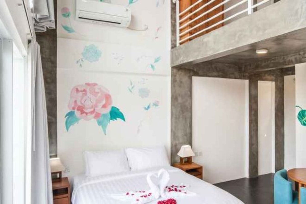 Quarto de hotel com cama, mesa de cabeceira, parede com arte floral e varanda.