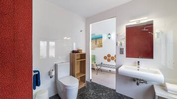 Casa de banho moderna com sanita branca, um prateleira de madeira, lavatório branco e zona de duche.