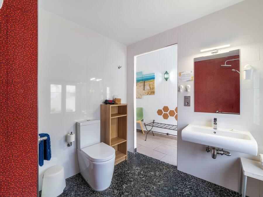 Casa de banho moderna com sanita branca, um prateleira de madeira, lavatório branco e zona de duche.