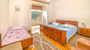 Quarto com cama de madeira, uma cama menor, mesa de cabeceira, abajur e vista para uma paisagem montanhosa pela janela.