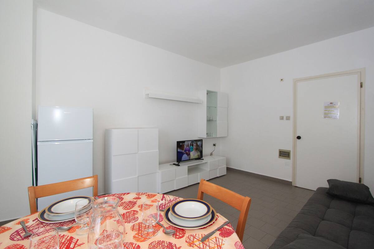 Uma área de refeições com uma mesa posta para dois, uma televisão em um armário branco e uma porta com um aviso.