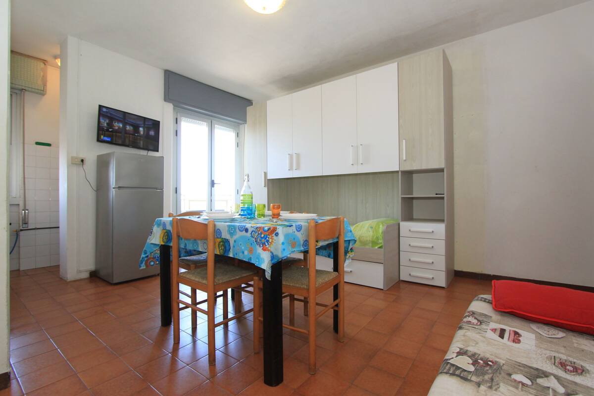 Cozinha compacta com mesa de jantar, cadeiras, geladeira e televisão fixada na parede.
