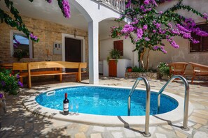 Uma área de piscina com um banco de madeira, uma garrafa de vinho e plantas em vasos.
