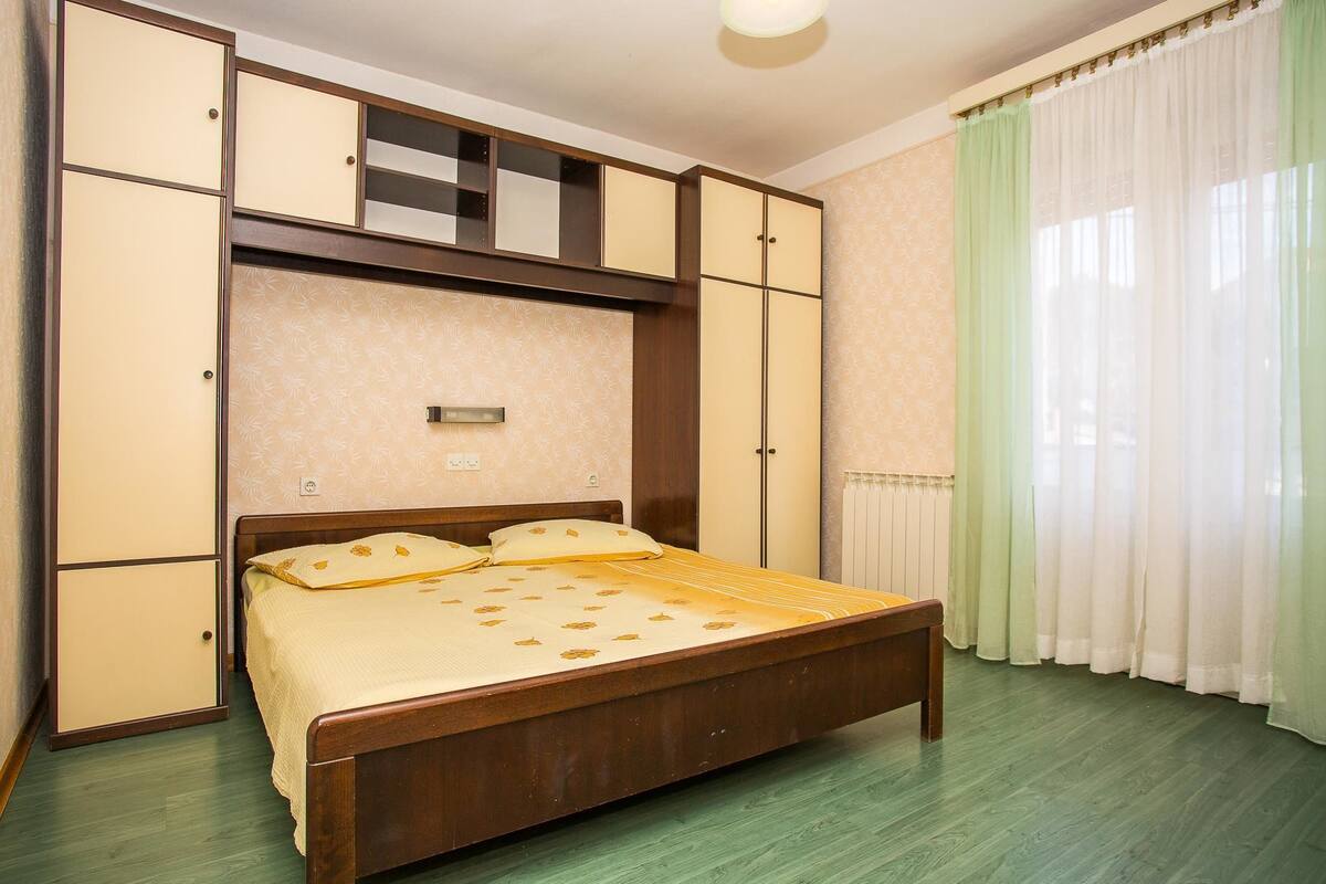 Quarto com cama de madeira, guarda-roupa com vários compartimentos e radiador.