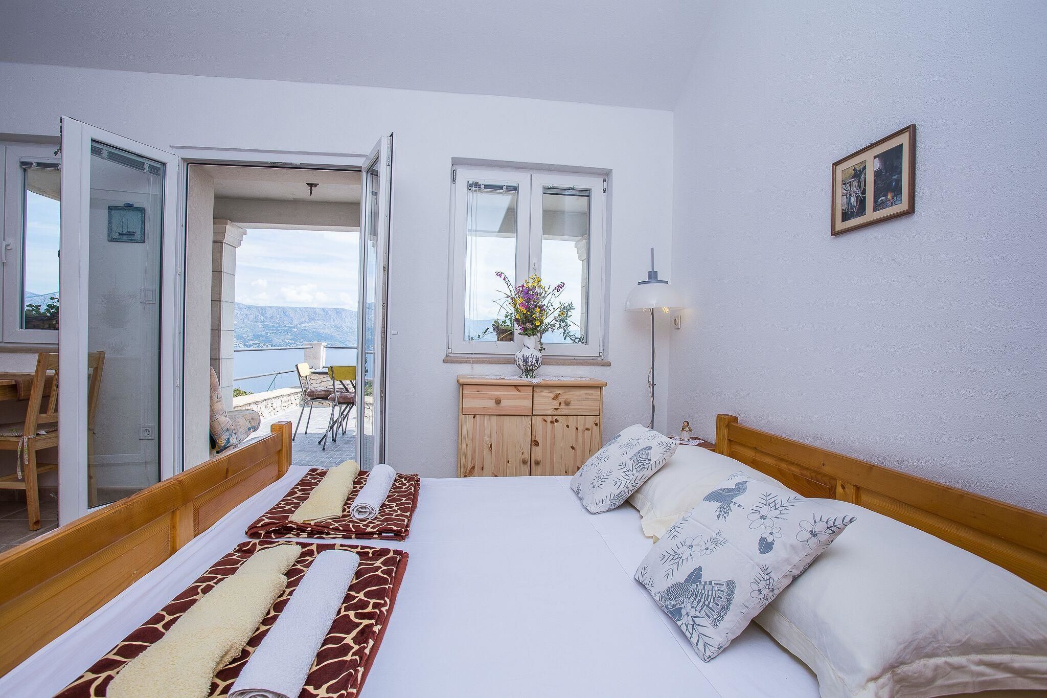 Quarto com cama, um banco de madeira, uma escrivaninha e vista para o exterior.