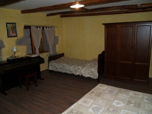 Quarto com uma cama de solteiro, um guarda-roupa de madeira, uma mesa com abajur e uma parede de pedra.