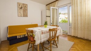 Um quarto acolhedor com piso de madeira, um sofá, uma mesa de jantar com cadeiras, um vaso de planta e uma porta de vidro deslizante que dá para uma varanda.