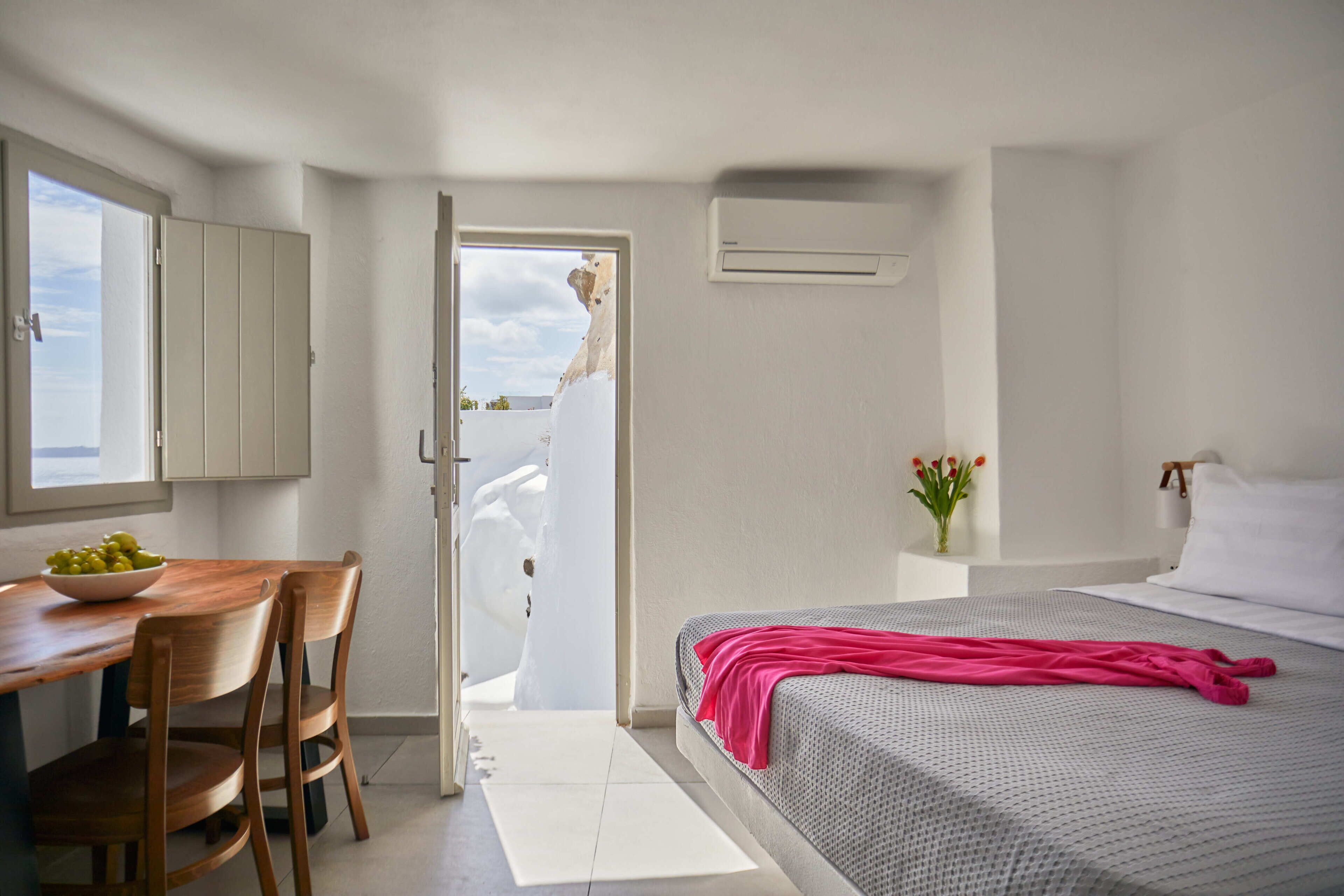 Quarto com cama, escrivaninha com cadeiras, janela e porta para o exterior.