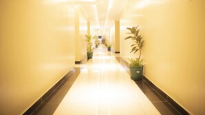 Um corredor bem iluminado e extenso, com plantas em vasos em ambos os lados e piso de azulejos.