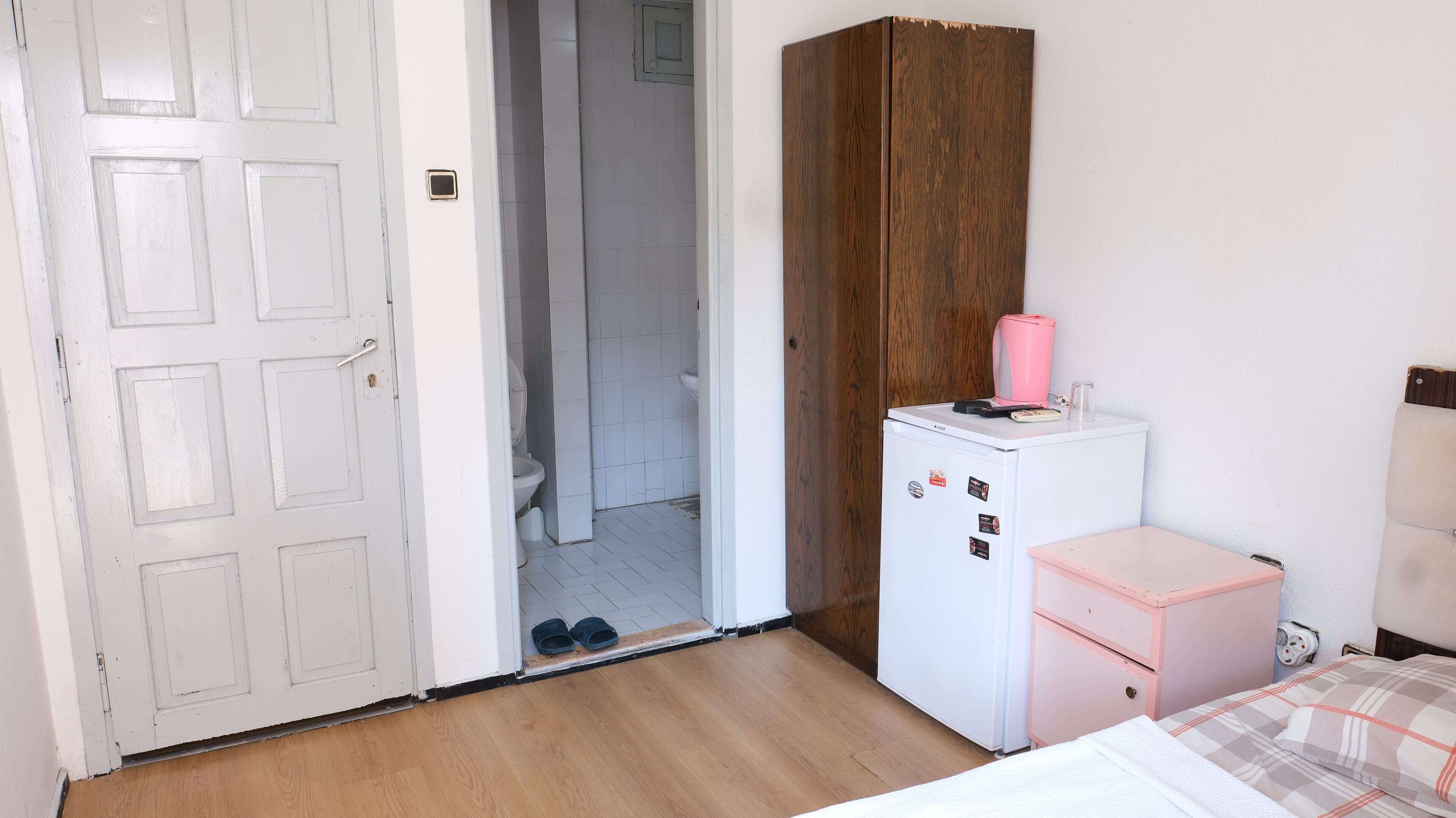 Quarto com guarda-roupa de madeira, um pequeno armário rosa e cama com colcha xadrez.