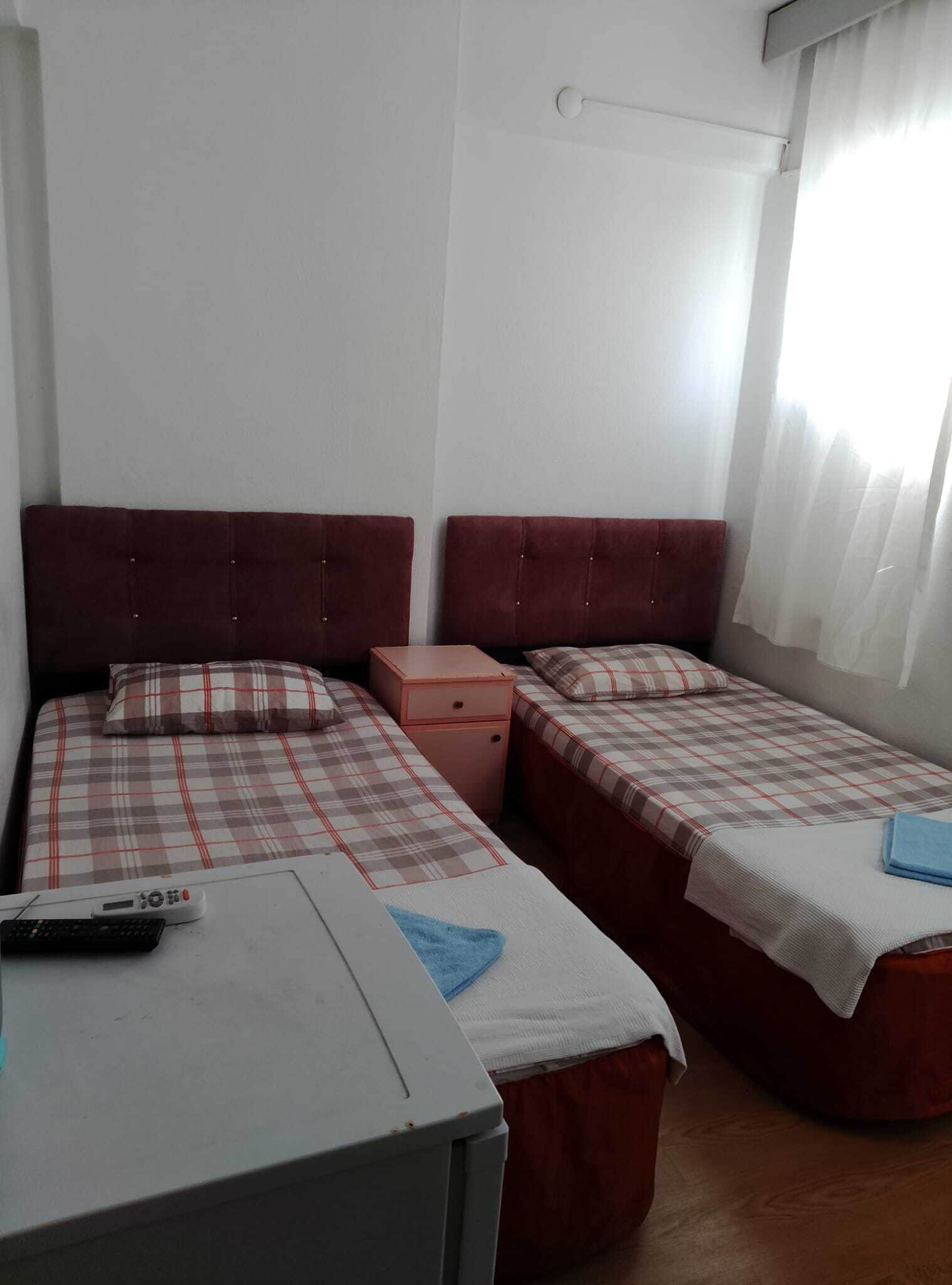 Quarto com duas camas, mesa de cabeceira, escrivaninha com computador e janela com cortinas.