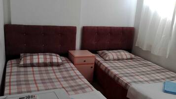 Quarto com duas camas, mesa de cabeceira, escrivaninha com computador e janela com cortinas.