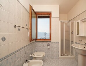 Casa de banho com sanita, bidé e lavatório. Tem uma janela com vista para montanhas e linhas de eletricidade.