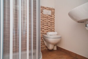 Uma casa de banho com parede revestida em azulejos, sanita e zona de duche.