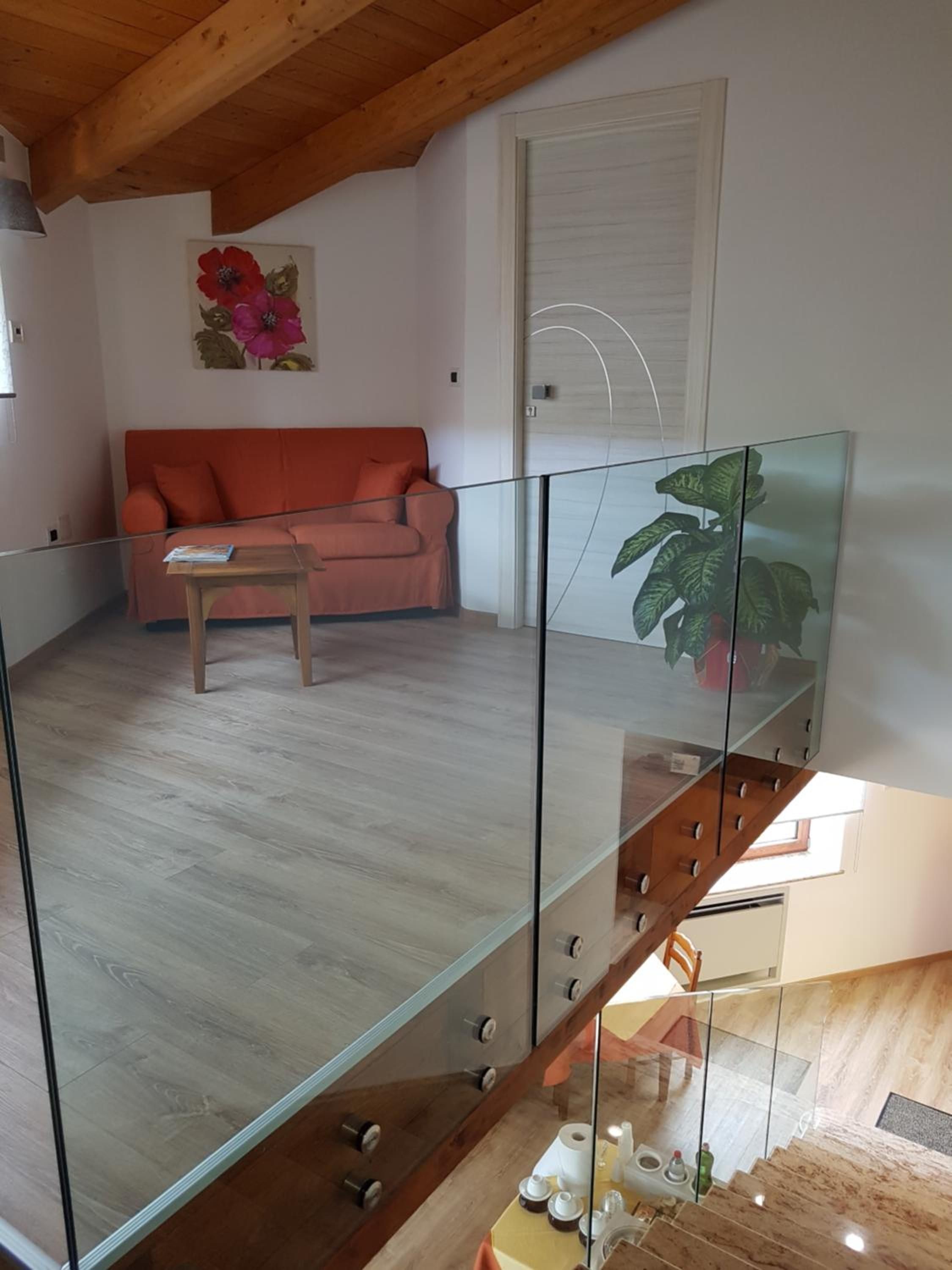 Interior moderno com teto de madeira, guarda-corpo de vidro, um sofá e uma planta.