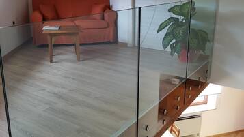 Interior moderno com teto de madeira, guarda-corpo de vidro, um sofá e uma planta.