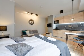 Quarto de hotel moderno com uma cama grande, uma escrivaninha, uma cozinha compacta e uma televisão.