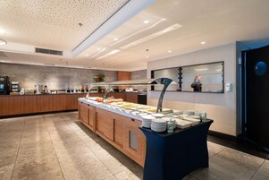Disposição de buffet com diversos alimentos, uma máquina de café e um balcão com visor digital.