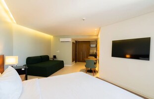 Quarto de hotel com cama, escrivaninha, cadeira, televisão e cozinha compacta.
