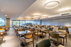 Uma ampla sala de jantar com várias mesas e cadeiras, janelas grandes e um design moderno no teto.