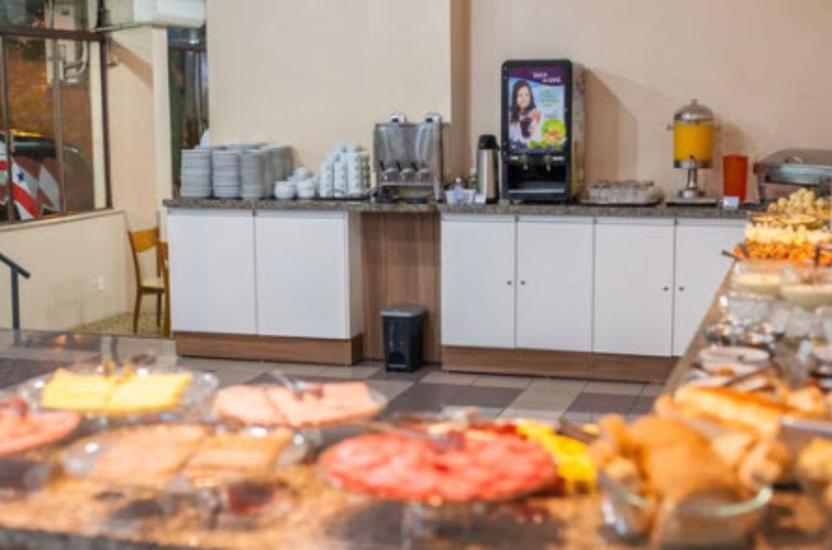 Disposição de buffet com diversos alimentos, uma máquina de café e um laptop no balcão.