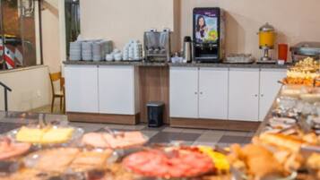 Disposição de buffet com diversos alimentos, uma máquina de café e um laptop no balcão.