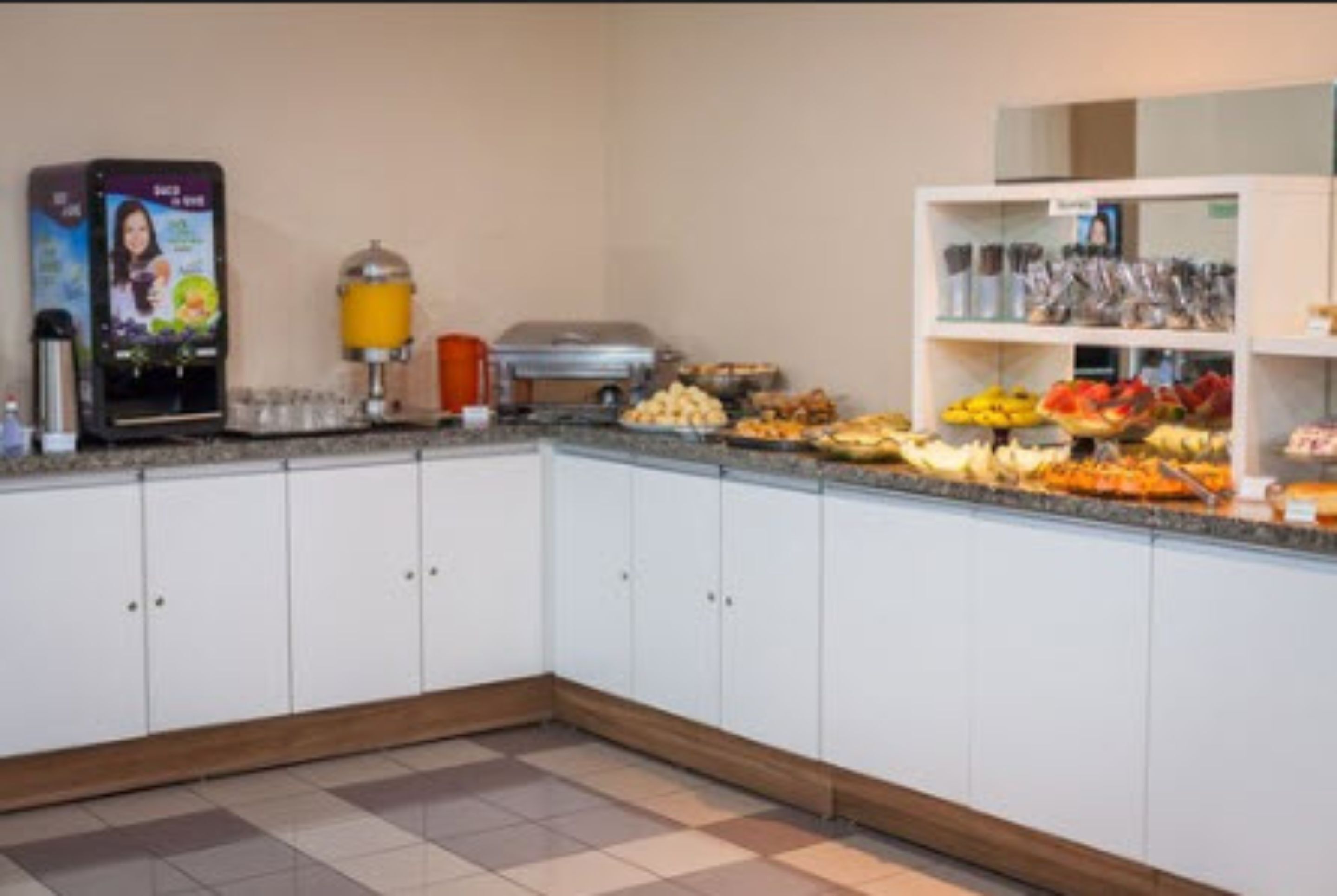 Disposição de buffet com diversos tipos de comida, um dispensador de bebidas e uma geladeira com visor digital.