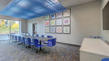 Uma sala de conferências com uma mesa comprida, cadeiras azuis, carpete estampado e quadros nas paredes.