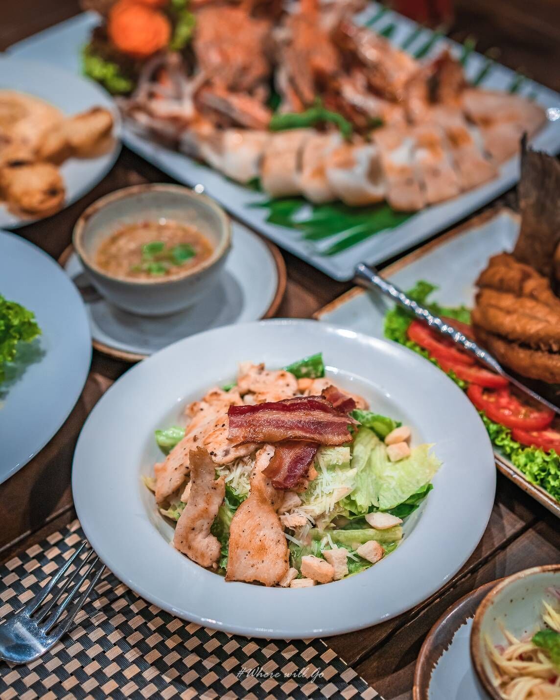 Uma mesa com diversos pratos, incluindo uma salada com bacon, frango grelhado e outros alimentos.