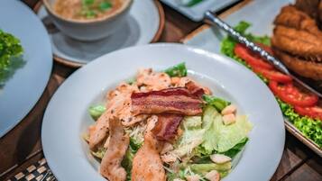 Uma mesa com diversos pratos, incluindo uma salada com bacon, frango grelhado e outros alimentos.