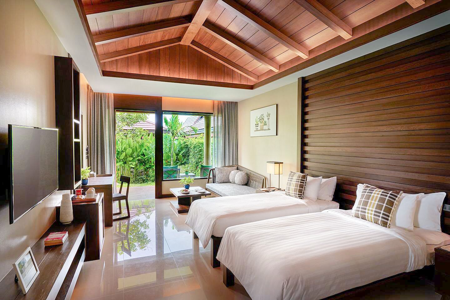 Quarto de hotel com duas camas, televisão, escrivaninha com cadeira e vista para o verde lá fora.