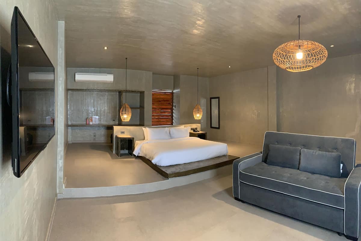 Quarto moderno com cama, sofá e luminária pendente.