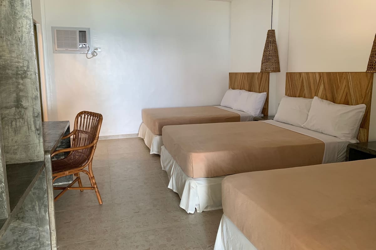 Quarto de hotel com duas camas, uma cadeira, uma mesa e ar condicionado fixado na parede.