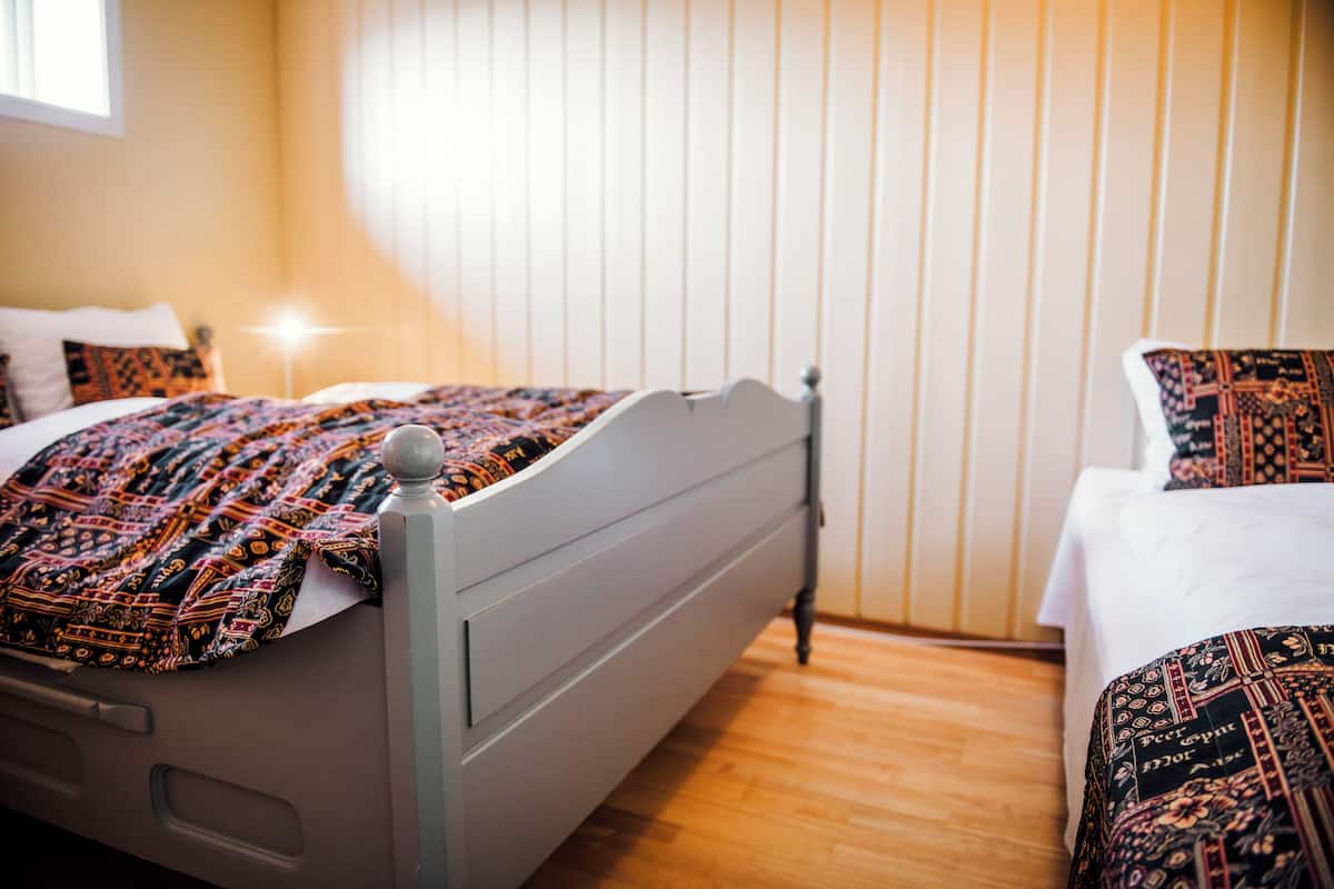Quarto com cama, mesa de cabeceira e janela com persianas.