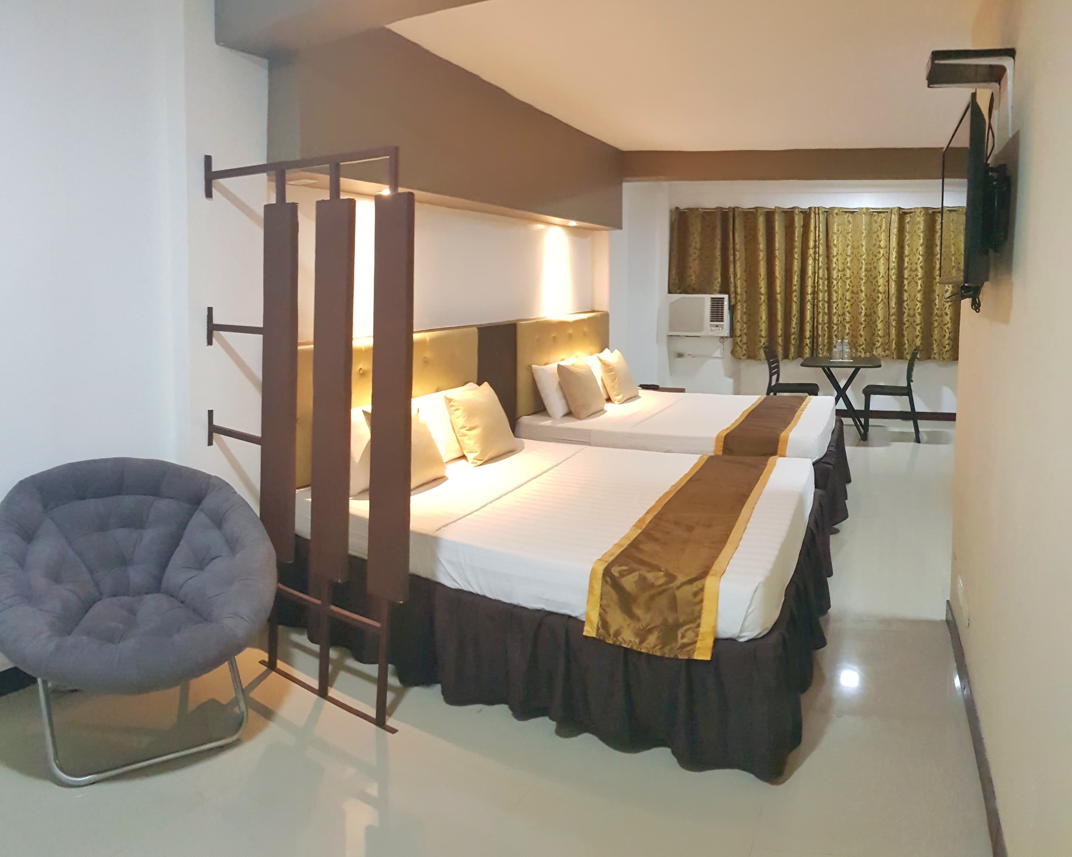 Quarto de hotel com duas camas, uma cadeira, um divisória, unidade de ar condicionado e uma mesa com cadeiras.