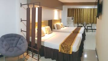 Quarto de hotel com duas camas, uma cadeira, um divisória, unidade de ar condicionado e uma mesa com cadeiras.