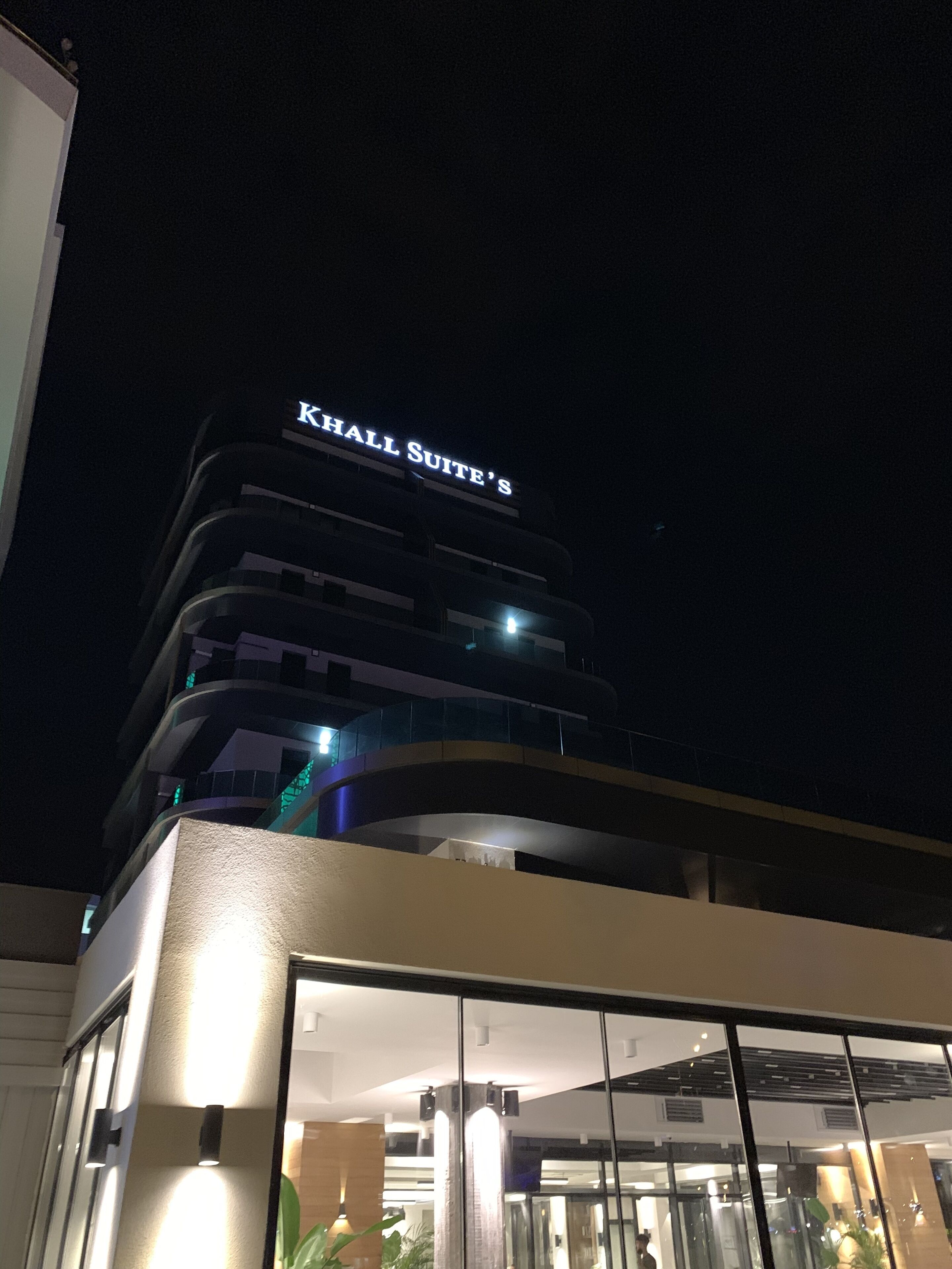 Um hotel chamado "Khal Suite's", com design arquitetônico moderno, vários andares e uma placa iluminada de destaque.