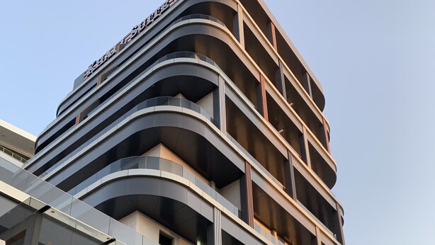 Um edifício de vários andares com design arquitetônico moderno, apresentando varandas curvas e fachada de vidro.