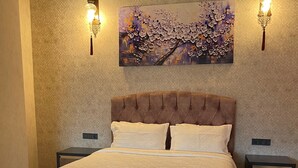 Quarto com cama grande, duas mesas de cabeceira, um quadro na parede e duas arandelas.
